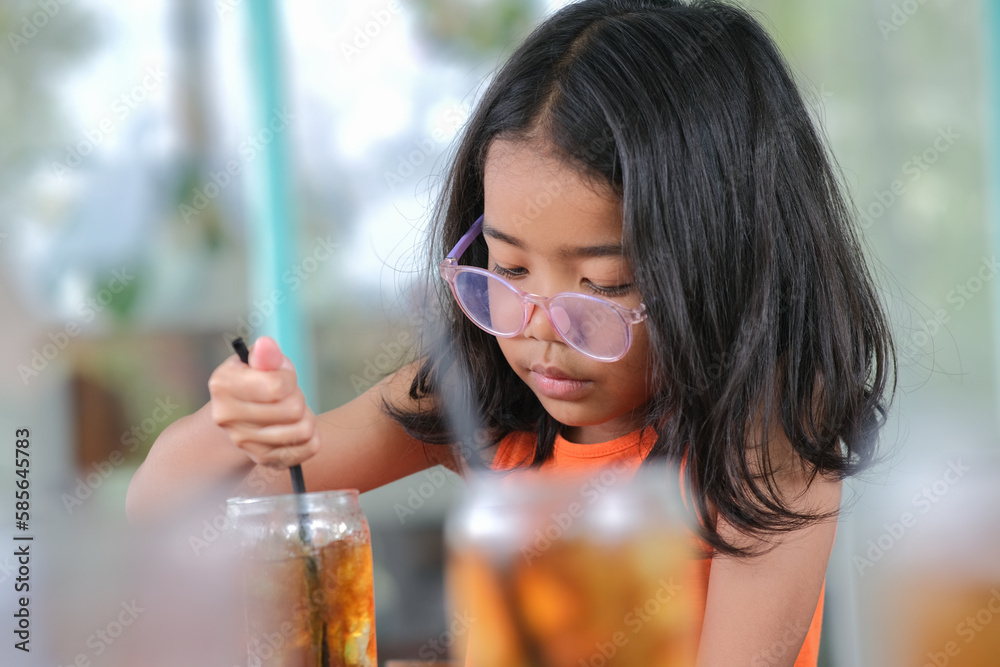 Facial expression of little female kid sitting alone drinking iced ...