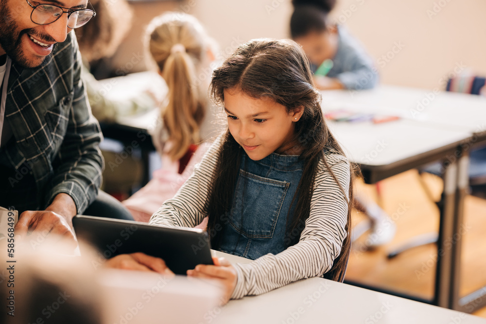Teacher shows a student how to use a digital tablet in an elementary ...