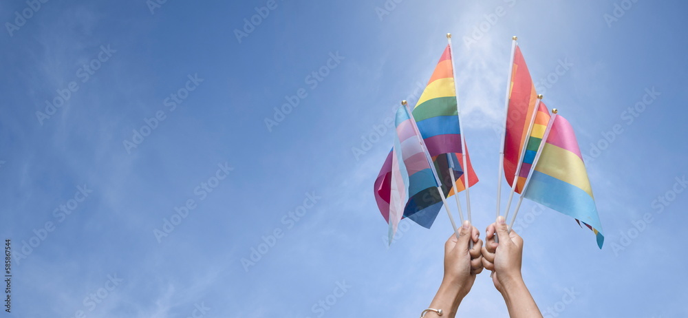 Rainbow flags showing in hands against clear bluesky, copy space ...