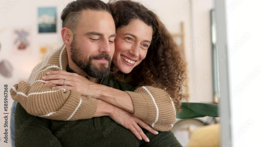 Woman embracing her husband while working from home in his workspace on a computer. Love, care ...