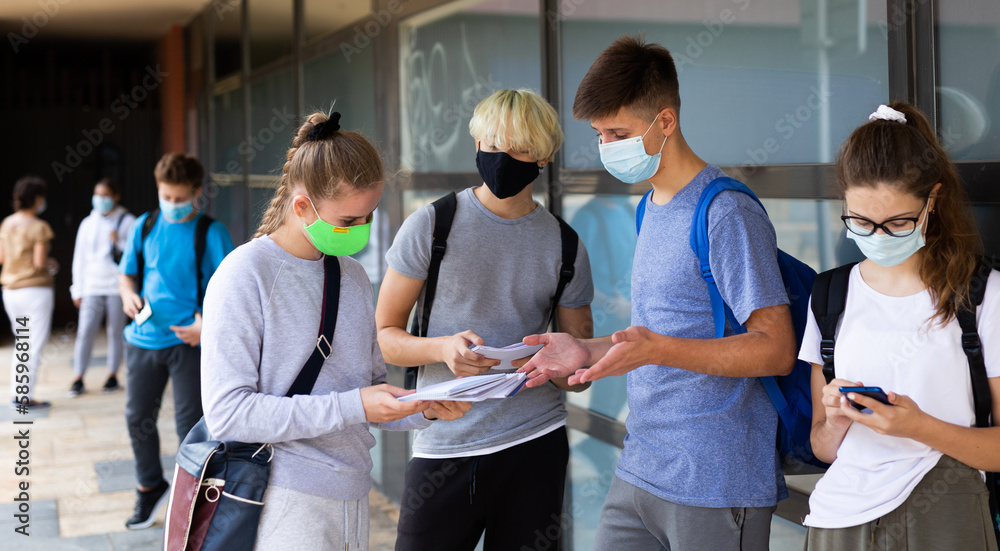 Teen students in medical face masks standing with workbooks in ...