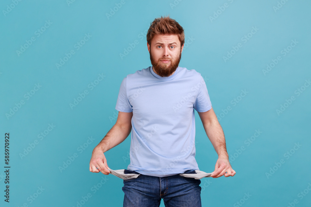 Man in blue T-shirt showing empty pockets and looking frustrated about ...