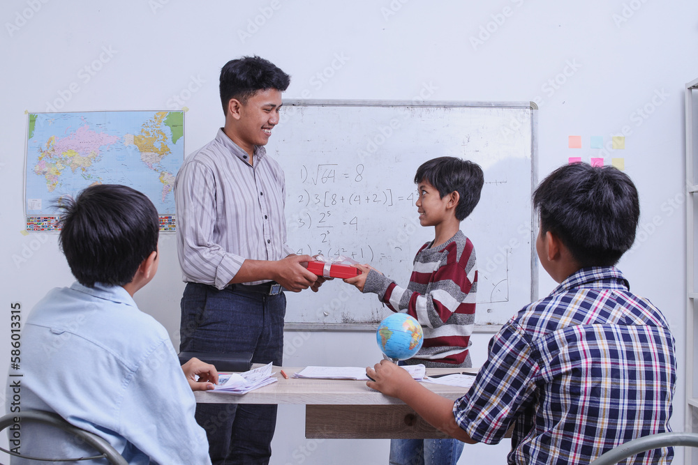 Potrait of teacher giving present to smart school boy in classroom ...