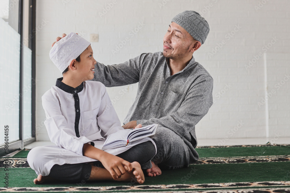 Portrait of happy Muslim father with son reading the Quran and praying ...