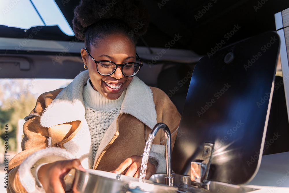 smiling african american woman cooking in camper van during a nomadic ...