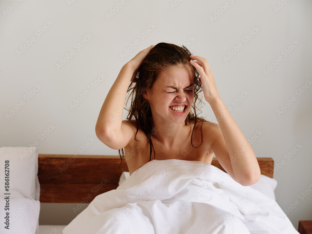 An angry woman sits on a bed in the bedroom and covers her body with a ...