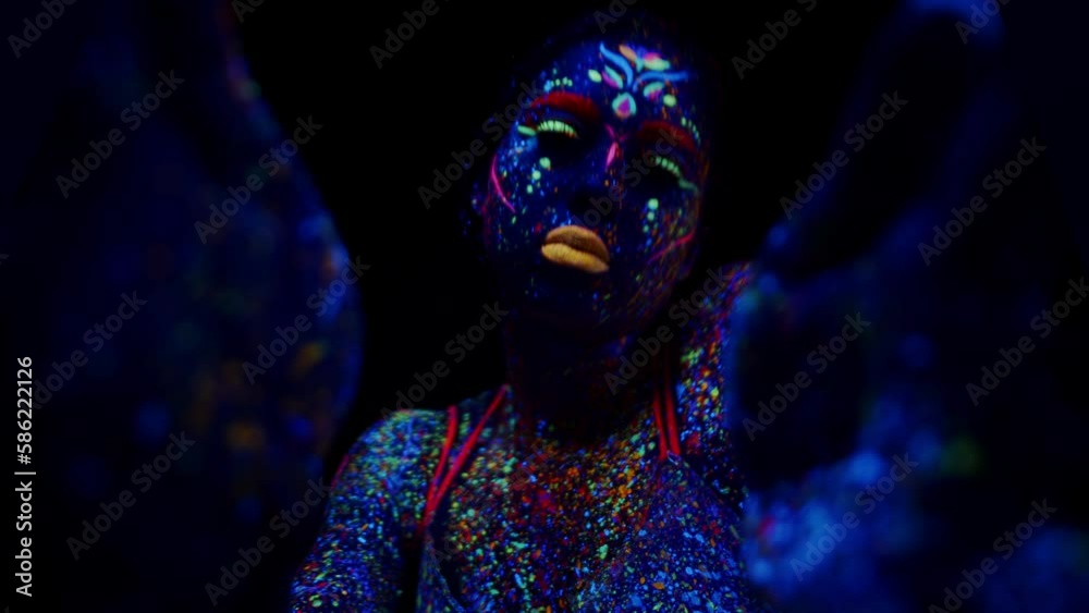 Young female performer with a fluorescent body painting stretches out ...