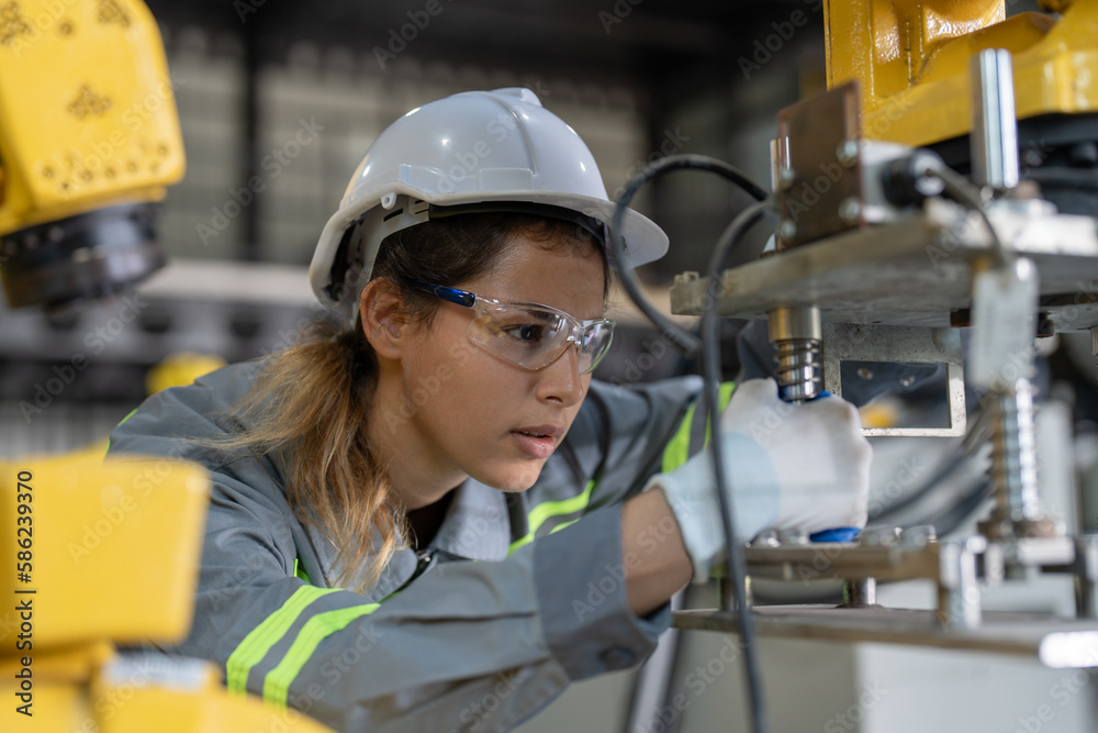 Female engineer checking and maintaining robot arms machine at factory. Technician woman in ...