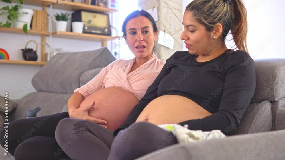 Two pregnant women on their 40´s happily talking at home sitting on the ...