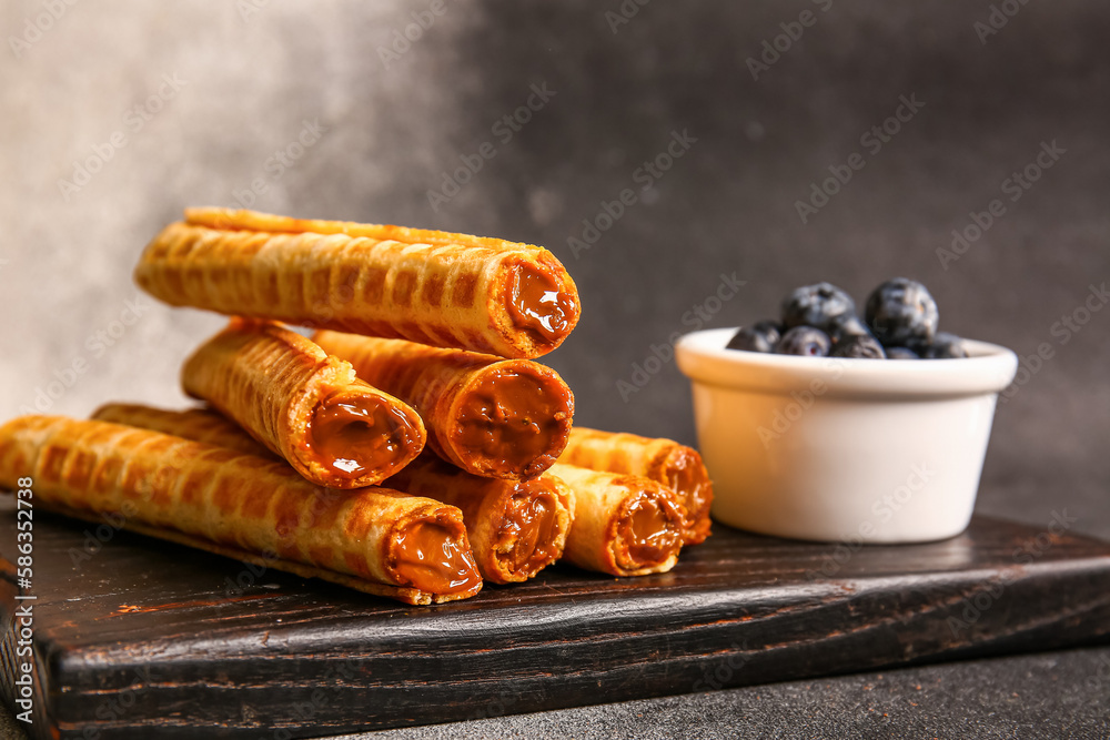 Board of wafer rolls with boiled condensed milk and blueberries on grey ...