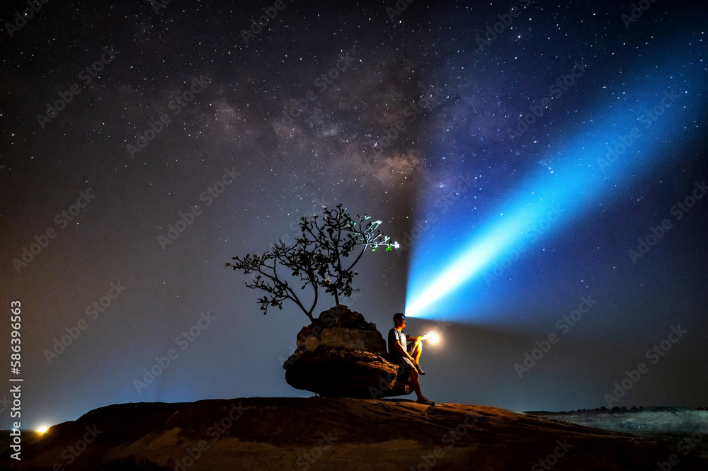Man tourist with flashlight on the rock at night. Space background with ...
