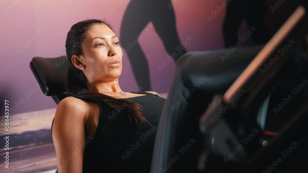 Young woman training legs muscles on leg press machine at the gym side ...