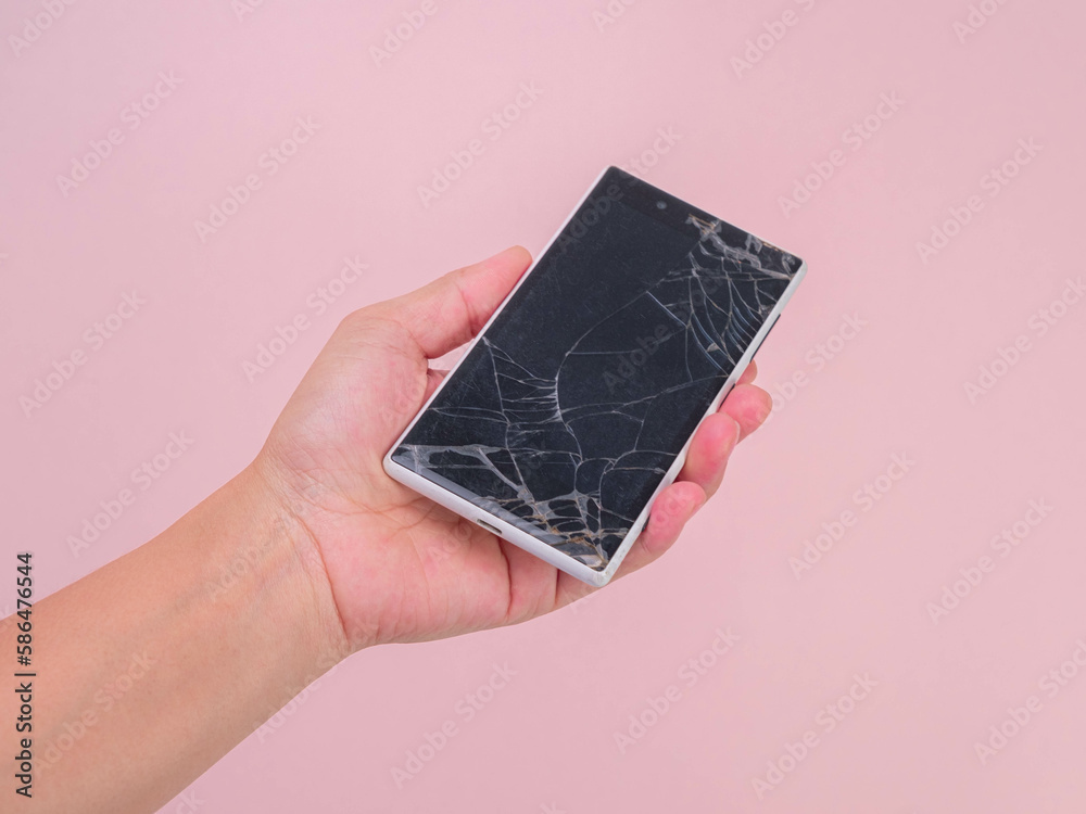 Close-up of hand holding mobile phone with broken touch screen on pink ...