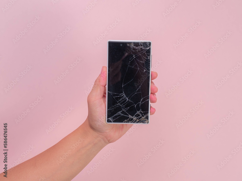 Close-up of hand holding mobile phone with broken touch screen on pink ...