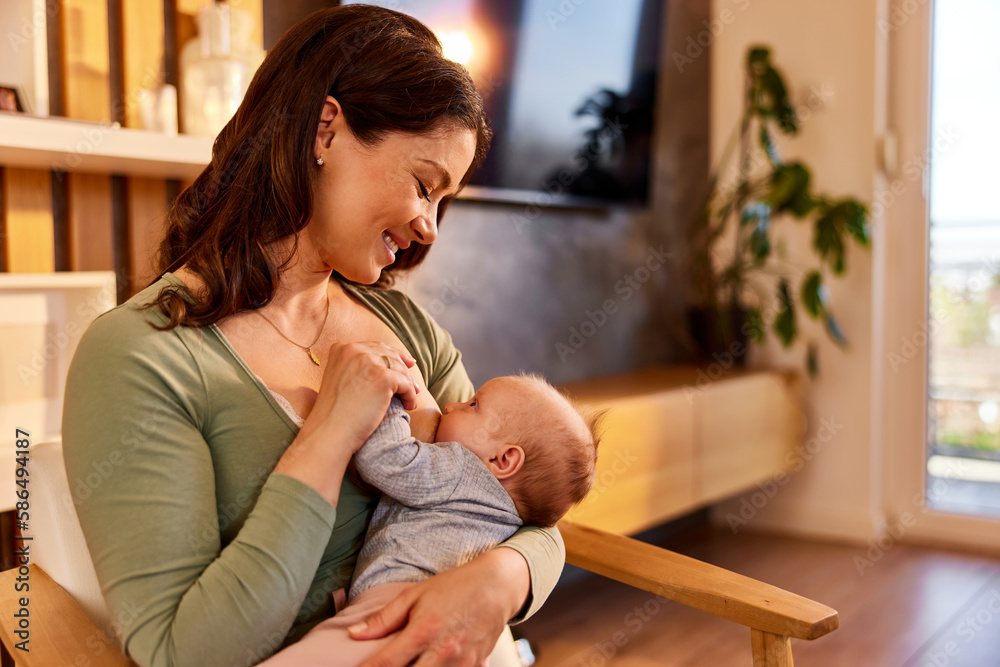 Happy mother holding her newborn child during breastfeeding at home ...