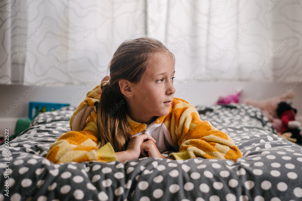 Foto de Tween girl in a giraffe onesie lying on her bed, looking away ...