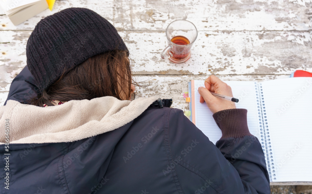 Young woman falling asleep while working and taking notes on wooden ...