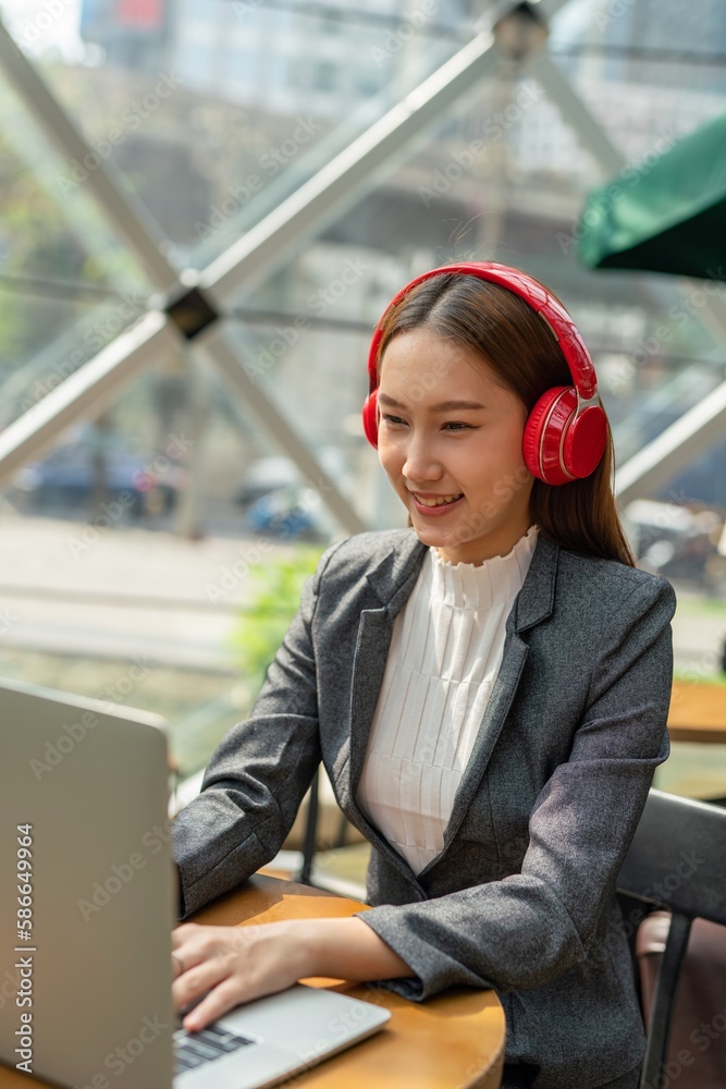Young asian businesswoman with a red headphone working on her computer ...
