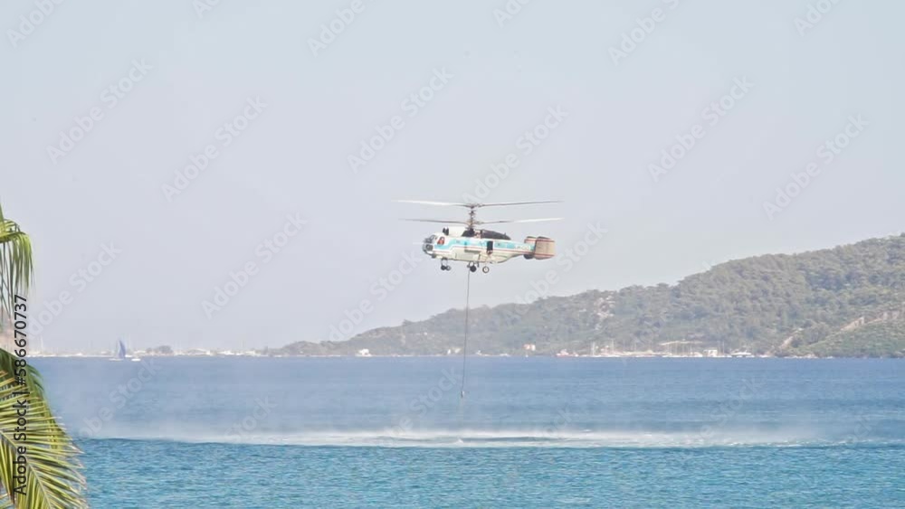 Fire rescue helicopter picks up bambi bucket of water in sea. Process ...