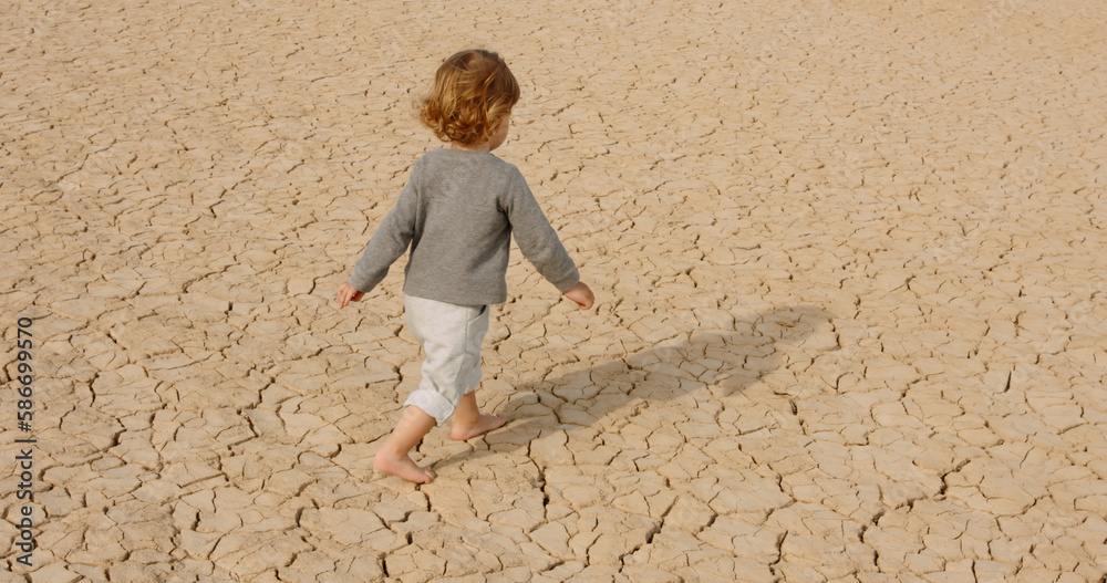 Funny caucasian baby boy running on deserted ground. Cracked soil land ...