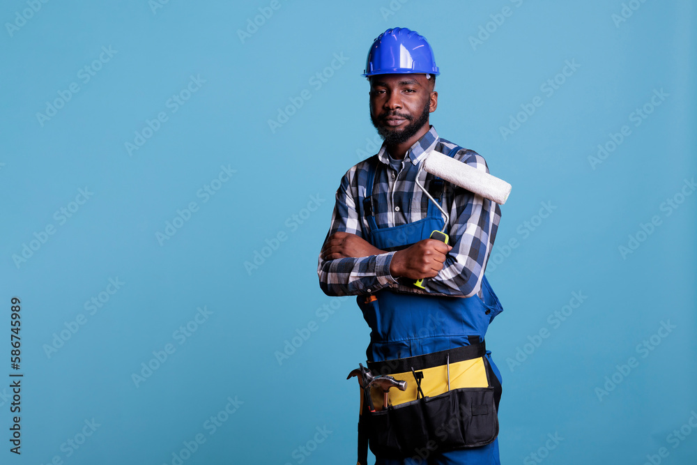 Professional painter looks at camera holding paint roller with overalls ...
