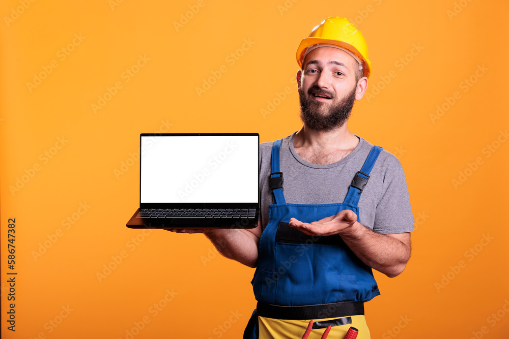 Cheerful builder showing laptop with white blank screen, holding pc ...
