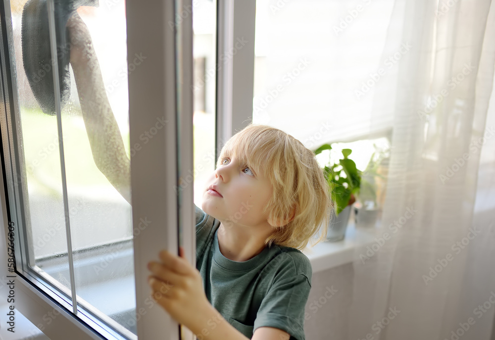 Cute little boy washing a window at home. Child helping parents with ...