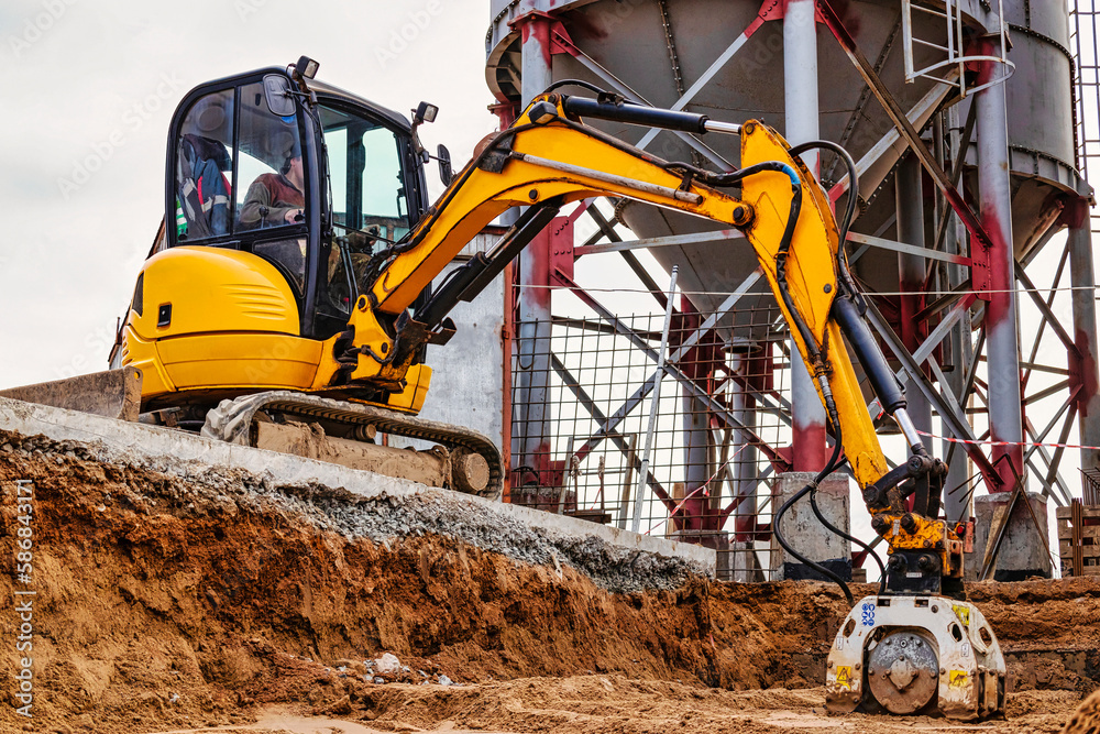 A mini excavator rams the ground with a vibrating plate. Laying of ...