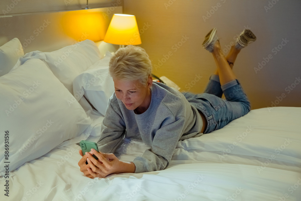 Blond woman texting on smartphone in bed at home at night before sleep ...
