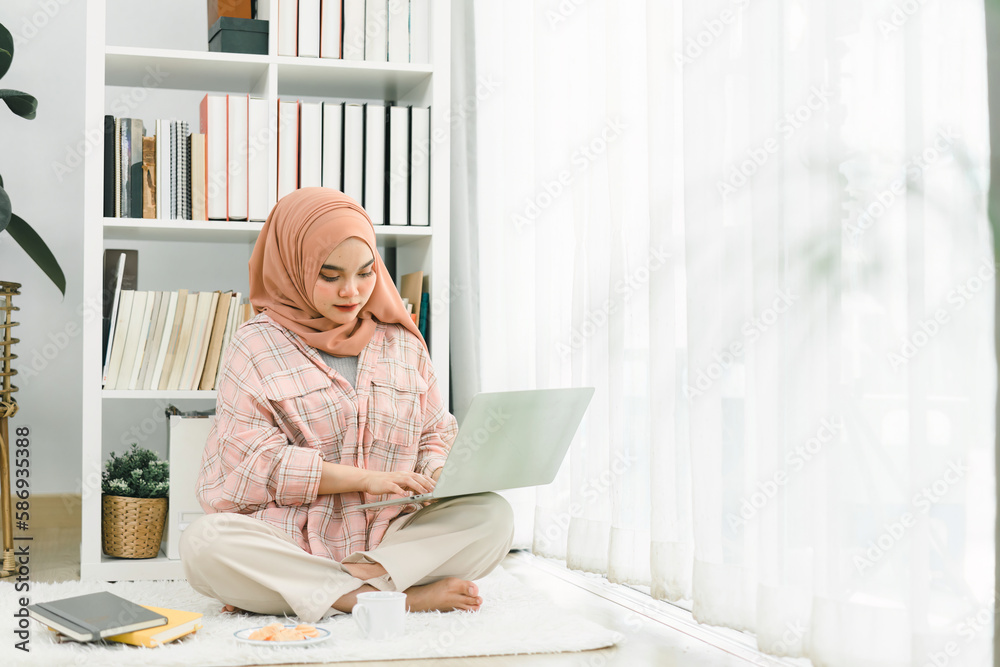 Beautiful Muslim girl wearing a hijab is working with a laptop computer ...