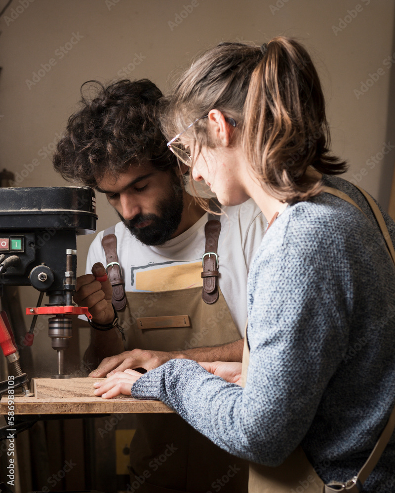 A young couple of carpenters working together in a small carpentry ...
