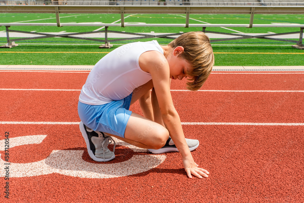 Young preteen boy track athlete in kneeling stance on sunny track ...
