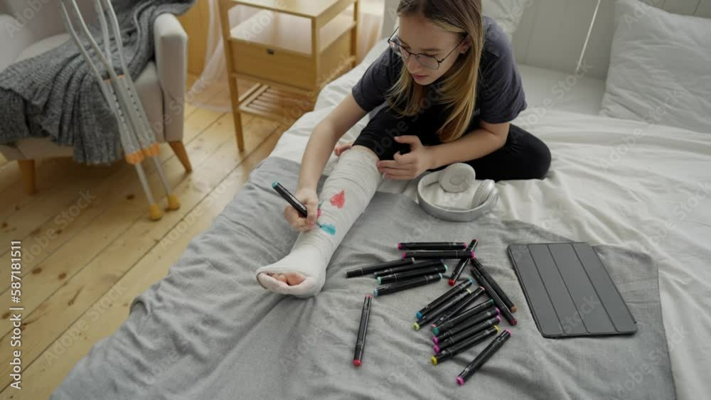 Unrecognizable girl with broken leg at bed on home draws with felt-tip ...