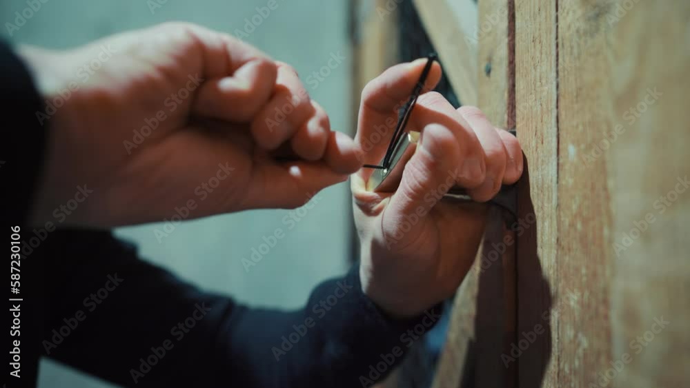 Man picking a lock on a storage cage door in a dimly lit warehouse ...