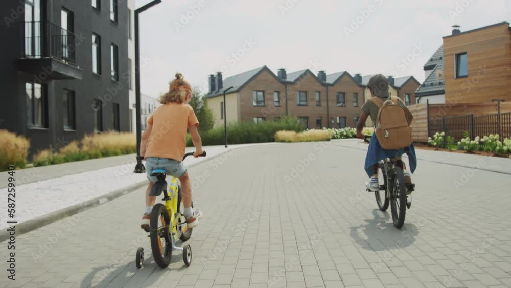 Full rear shot of two 9-year-old children in casual clothes pedaling on ...