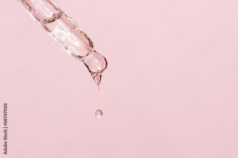 Cosmetic pipette with dripping liquid and drops on a pink background ...