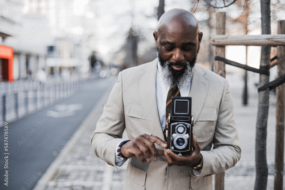 An aging man dressed elegantly holding an old TLR film camera. A ...
