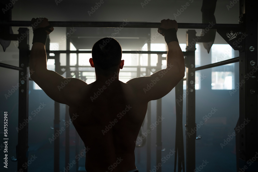 Fit shirtless man doing full chin-up exercise hanging on bar in sunny ...