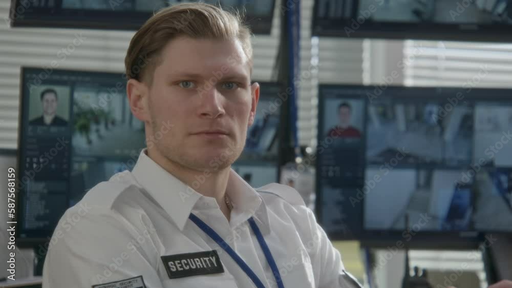 Security worker in uniform sits in observation room and looks at camera ...