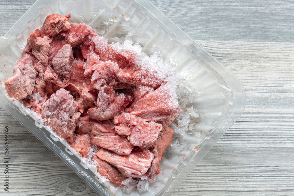 Frozen lean beef steak cubes in clear plastic tray packaging. On a grey ...