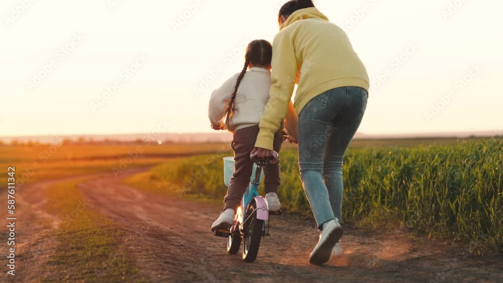 mother teaches child ride two-wheeled bicycle sunset. happy family ...