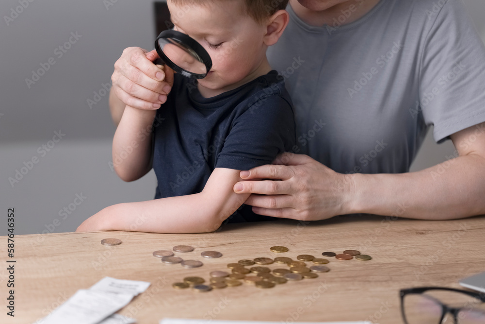 A little boy looks at coins through a magnifying glass. A child with ...
