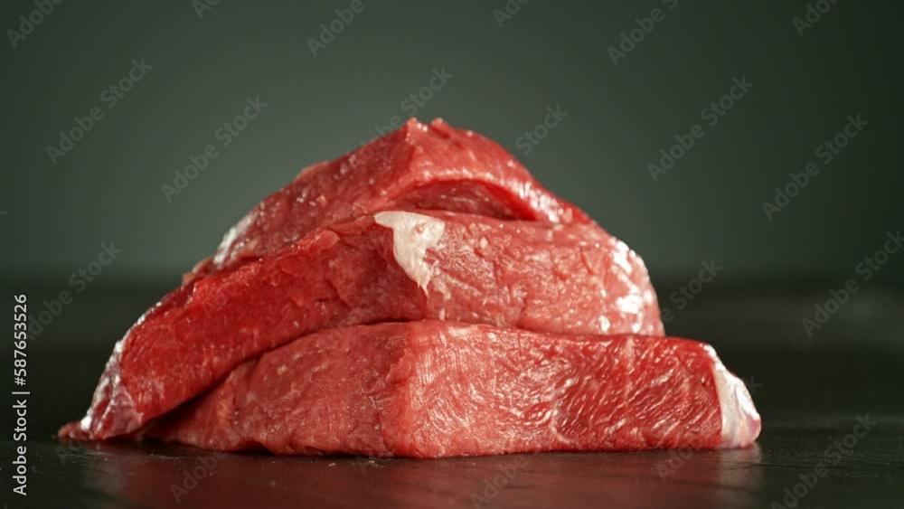 Flying pieces of raw beef steaks falling on table. Filmed on high speed ...