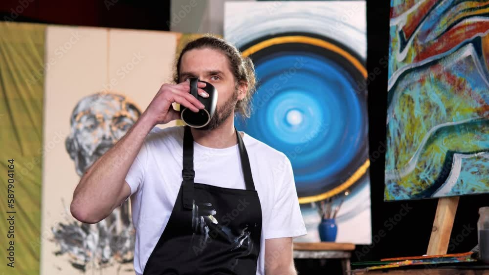 Contemplative artist dressed in a white t-shirt drinks coffee while ...