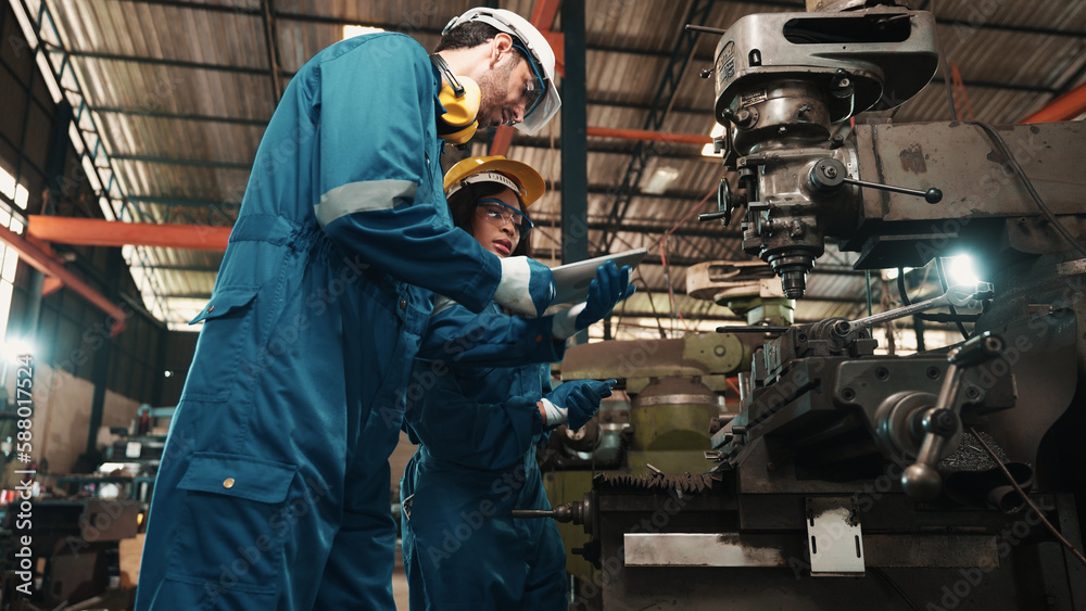 Two multiracial factory workers in safety wear are examining metal ...