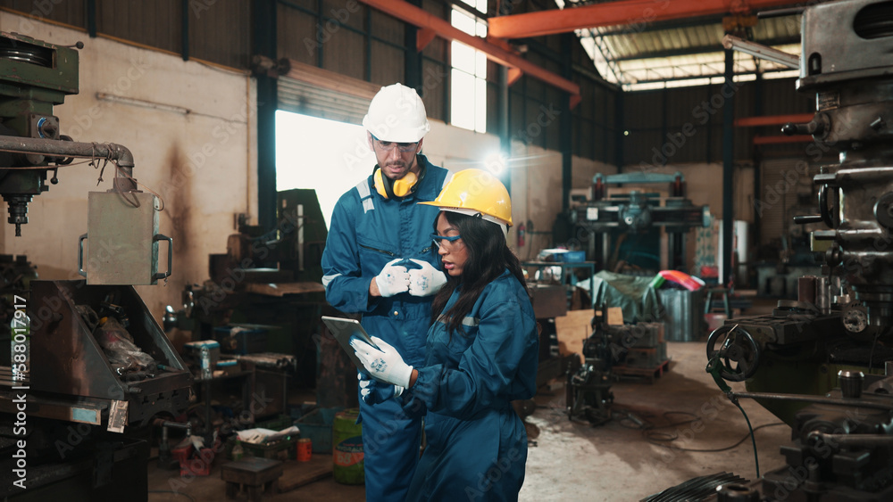 Two multiracial factory workers in safety wear are using a tablet to ...
