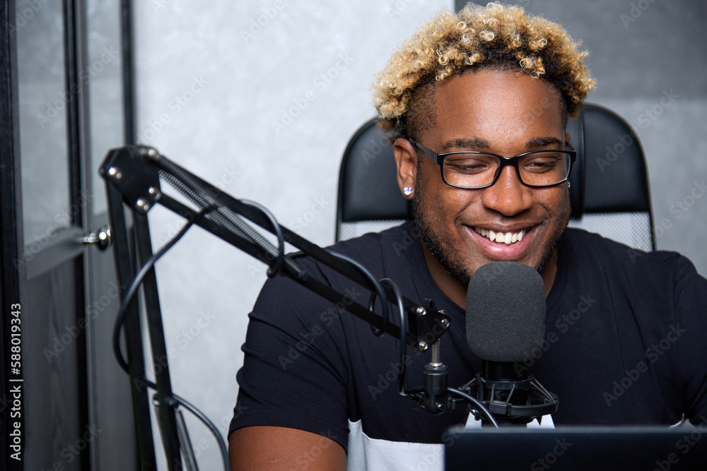 A cheerful black podcaster at the workplace with a professional ...