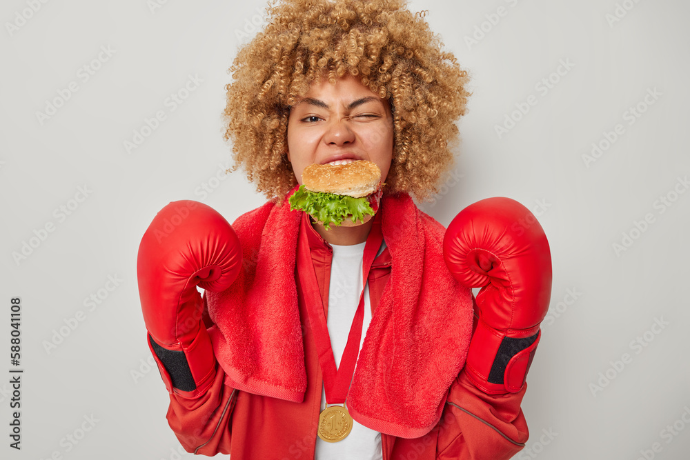 Foto Stock Indoor shot of female boxer winks eye eats tasty burger ...