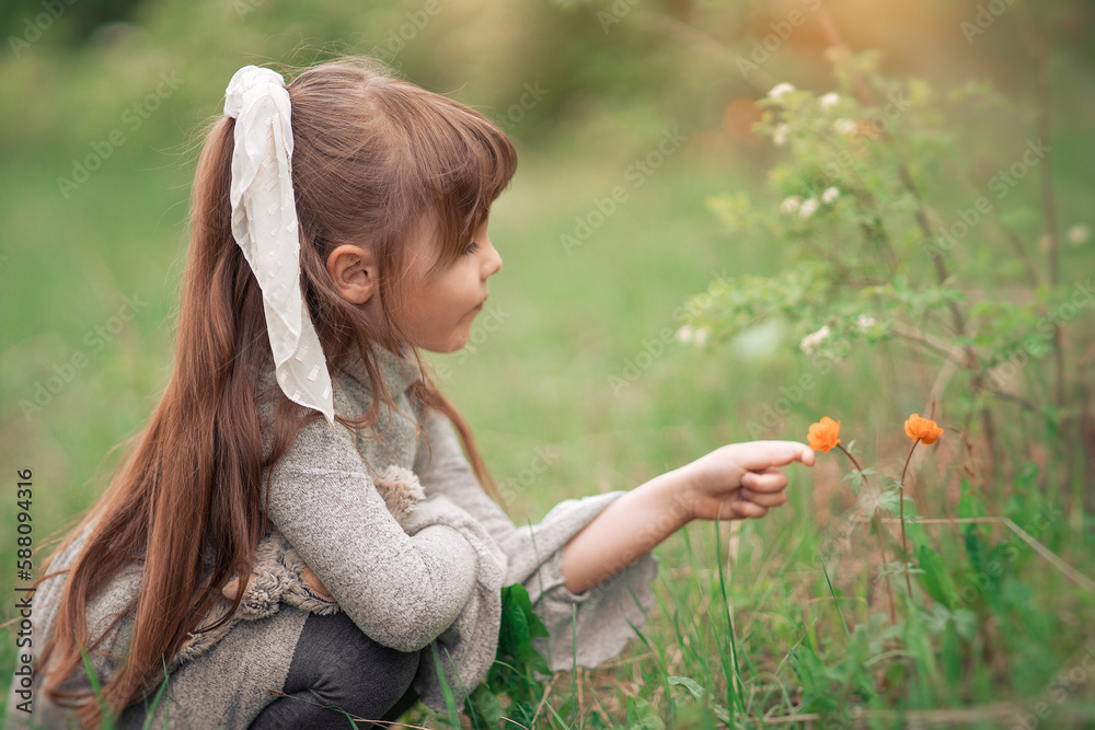 Little girl touch strokes orange flower in the park. Background summer ...