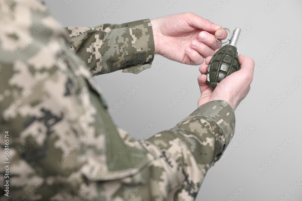 Soldier pulling safety pin out of hand grenade on light grey background ...
